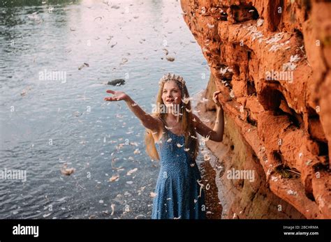 Young Woman In Crown From Shells Staying Near Red Sand Wall In River And Catching Feathers Stock