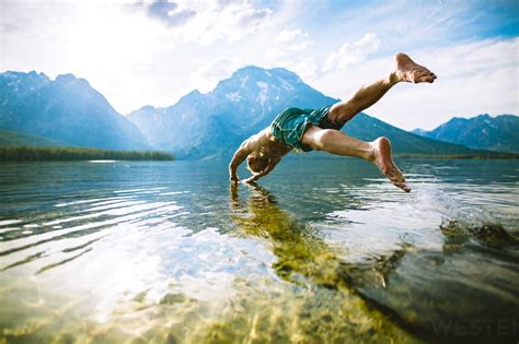 Man Diving Into Lake Against Mountains And Sky Stock Photo