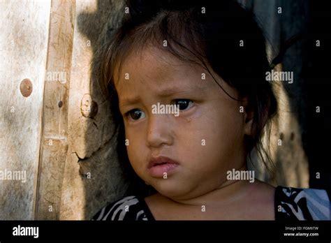 A Young Girl Living In Poverty Looks Outside Her Wood Home In Kampong