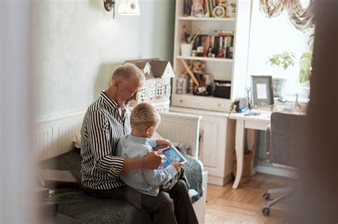 Grandfather And Grandson Using Digital Tablet While Sitting On Couch