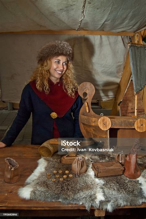 푸른 눈을 가진 소녀는 룬에 경이로움 중세 축제에서 바이킹 의상을 입은 금발 북부 민족의 정통 의류와 라이프 스타일 나무 테이블에 모피 고대의에 대한 스톡 사진 및 기타