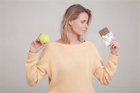 아름다운 젊은 금발 소녀는 초콜릿의 바와 그녀의 얼굴 주위에 녹색 사과를 보유하고 그녀는 선택을 할 수 없습니다 그녀는 노란색
