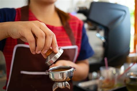 포터필터를 들고 있는 바리스타와 에스프레소 커피를 만드는 커피 탬퍼의 손 바리스타는 커피숍에서 탬퍼를 사용하여 분쇄 커피를 압착합니다 갈색에 대한 스톡 사진 및 기타 이미지