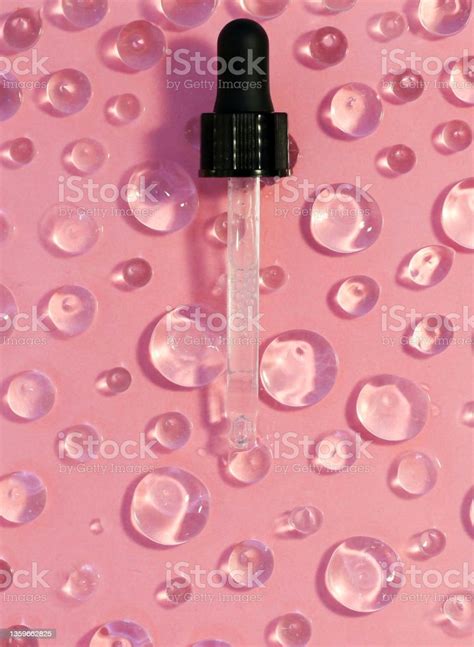 분홍색 배경에 유리 파이펫에서 히알루론산 세럼 또는 오일의 투명한 둥근 방울 유기농 에센스 미용 및 건강 제품의 세련된 컨셉