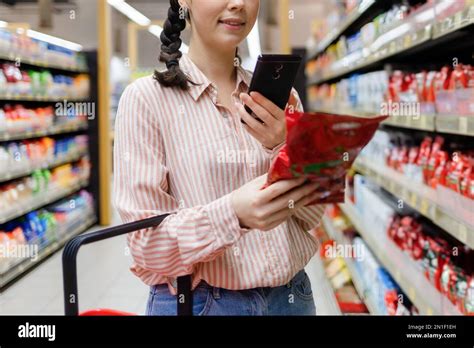 Close Up Of Caucasian Woman Scans Qr Code Of Product Using Smartphone Shelves With Food And