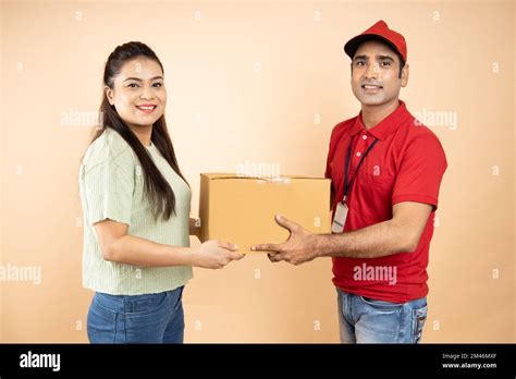 Indian Delivery Man Deliver Box Parcel Package To Woman Customer Standing Over Beige Studio