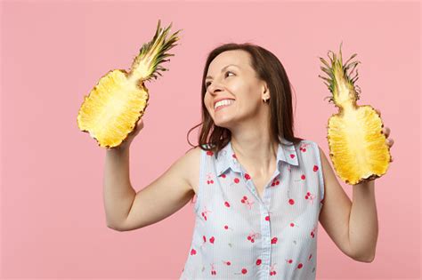 여름 옷에 멋진 젊은 여자 분홍색 파스텔 배경에 고립 된 신선한 잘 익은 파인애플 과일의 Halfs를 들고 옆으로 찾고 사람들은 생생한 라이프 스타일 휴식 휴가 개념입니다