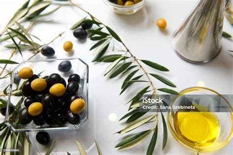 엑스트라 버진 올리브 오일로 채워진 클로즈업 유리 그릇 흰색과 검은색 올리브와 잎이 흰색 테이블 배경에 함께 있습니다 올리브 수확 시기와 농업 지중해 음식 컨셉 0명에 대한