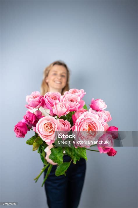밝은 회색 배경에 분홍색 모란 장미의 큰 꽃다발을 가진 젊은 금발 소녀 3 월 8 일 첫 데이트 얼굴에 감정 웃고있는 소녀 배경에 초점이 맞지 않습니다 감정 시리즈에 대한