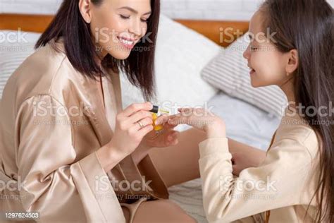 쾌활한 젊은 어머니는 집에서 침대에 그녀의 딸의 손톱에 광택을 적용 2명에 대한 스톡 사진 및 기타 이미지 2명 Covid