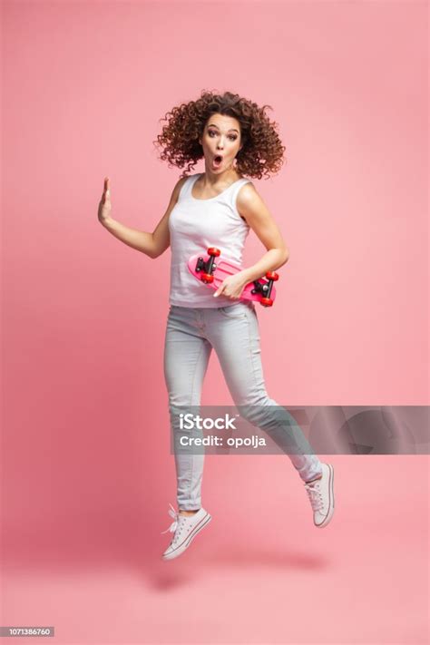 전체 길이 포즈와 점프 그리고 스케이트 보드 핑크 배경 위에 절연을 유지 하는 동안 멀리 보고 여름 옷을 입고 아름 다운 행복 한 여자의 초상화 갈색 머리에 대한 스톡 사진
