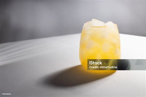 현대적인 심플한 추상적 스타일의 그라데이션 벽이 있는 흰색 테이블에 줄무늬 그림자가 있는 햇빛에 유리로 얼음을 곁들인 신선한 여름 차가운 오렌지 주스 감귤류 과일에 대한