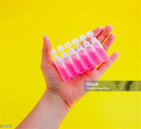 ピンクの液体薬を持つ女性の手の保持アンプルは黄色の背景に分離しました 1人のストックフォトや画像を多数ご用意 1人 カラー背景