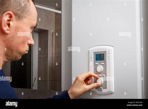 Men Regulate Temperature On Control Panel Of Central Heating Or DHW At Combi Boiler In Restroom