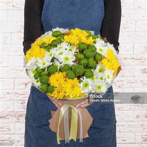 푸른 데님 앞치마에 젊은 꽃집 여자 흰색의 무리를 들고 녹색과 노란색 꽃 꽃 꽃다발 빛 벽돌 벽 배경 부케에 대한 스톡 사진 및 기타 이미지 Istock