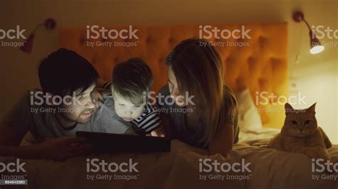 행복 한 가족의 작은 아들과 함께 재미 있는 고양이 집에서 침대에 누워 자기 전에 태블릿 컴퓨터에 소셜 미디어를 서핑 가정