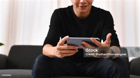 집에서 소파에서 휴식을 취하면서 스마트 폰으로 비디오를보고있는 웃는 남자의 자른 이미지 20 24세에 대한 스톡 사진 및 기타