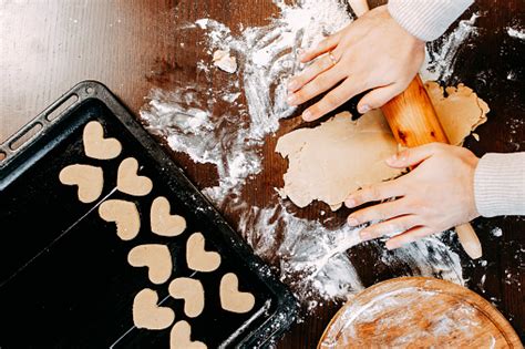 성 발렌타인 데이를 위한 하트 모양의 쿠키 남자는 세인트 발렌타인 데이에 대한 심장 모양 쿠키를 굽고있다 남자는 밀가루를 들고 식탁에 반죽을 굴리고 있다 나무 롤링 핀