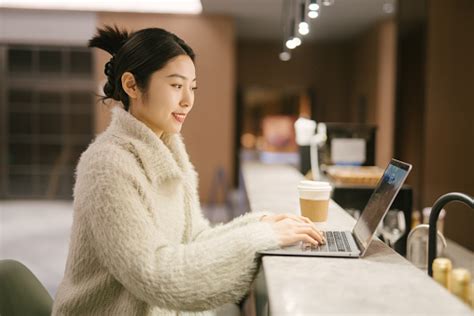 한 20대 젊은 아시아 여성이 낮 시간에 커피를 옆에 두고 카페에서 노트북으로 작업을 하고 있습니다 20 29세에 대한 스톡
