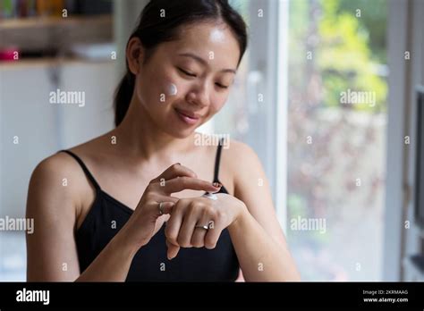 Smiling Ethnic Female Spreading Cream On Hands In Morning At Home On