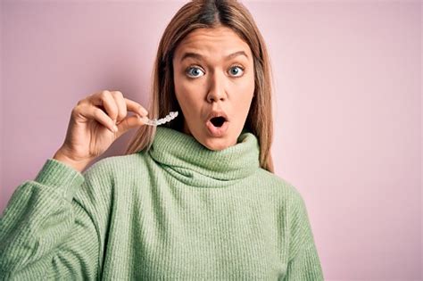 고립 된 분홍색 배경 위에 서있는 정렬기를 들고있는 젊은 아름다운 여성은 깜짝 얼굴로 충격에 무서워하고 두려움과 두려움 표현으로