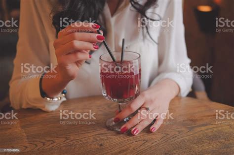 여자는 커피 숍에서 멀드 와인을 마신다 흰색 셔츠와 레스토랑 카페에서 알코올 레드 와인 한 잔을 들고 손톱에 적갈색 바니시에
