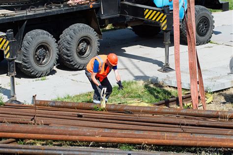 안전모와 눈에 잘 띄는 조끼를 입은 슬링어는 여름날 열린 창고에서 가스화를 위해 금속 파이프를 내립니다 무거운에 대한 스톡 사진 및 기타 이미지 Istock