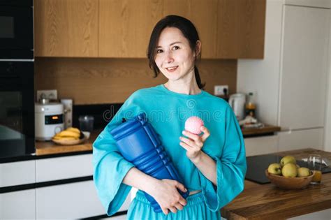 Young Adult White Woman Smiling In A Modern Kitchen While Holding A