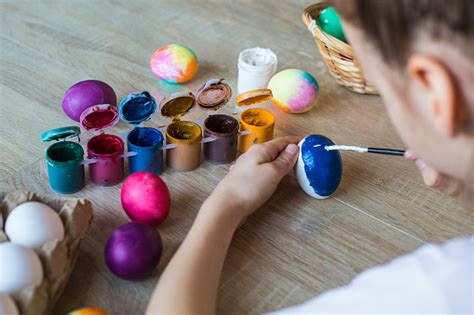 흰색 티셔츠를 입은 소녀는 페인트와 브러시 클로즈업으로 부활절 색 달걀을 칠합니다 부활절 봄 페인트 달걀 아이는 페인트 칠한 알을 들고 있습니다 행복한 아이가 부활절을