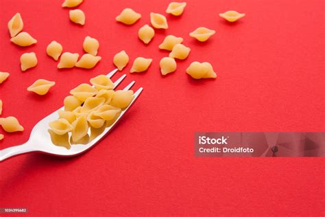 Silver Fork With Small Conchiglie On A Red Background With Pasta Around