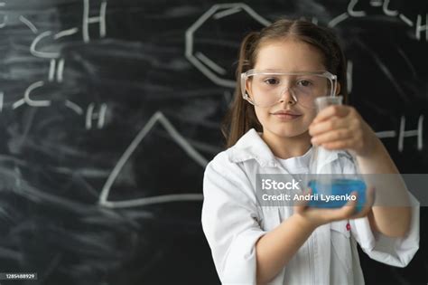 수업에서 화학 수업에서 칠판 근처의 귀여운 어린 소녀 손에 파란색 액체와 플라스크를 잡아 Stem 주제에 대한 스톡 사진 및