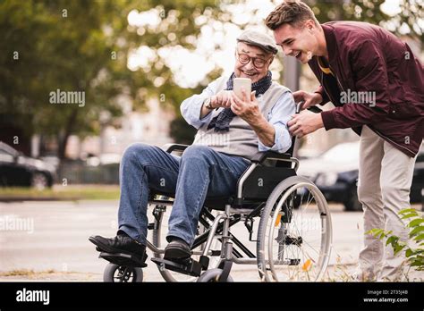 Laughing Senior Man In Wheelchair And His Adult Grandson Looking