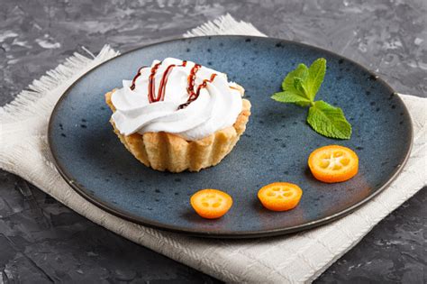 리넨 냅킨과 검은 콘크리트 배경에 Kumquat 슬라이스와 민트 잎과 파란색 세라믹 접시에 휘핑 계란 크림 케이크 측면 보기 0