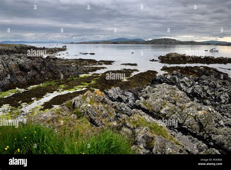 Sand Beach And Rocky Shore Under Clouds On Isle Of Iona With Boats On