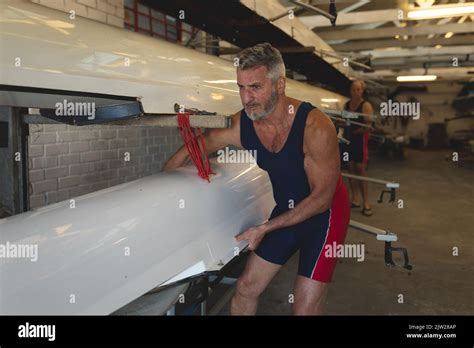 Senior Caucasian Male Rower Carrying Boat In The Boat Warehouse Stock