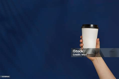 네이비 블루 배경에 커피 또는 차 종이 컵 종이 컵을 들고 있는 남성 손의 모형 빈 폴리스티렌 커피 머그잔의 전면보기 모형 없애