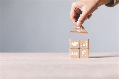 손은 사업 전략과 행동 계획에 대한 아이콘으로 나무 블록을 쌓고 있습니다 다트 보드와 화살표는 비즈니스 목표 목표를 설정합니다