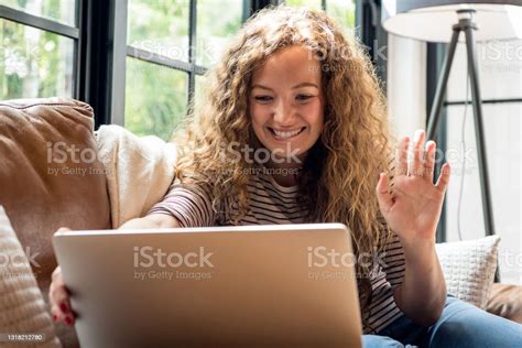 예쁜 백인 여자 미소와 카메라에 손을 흔들어 집에서 거실에서 소파에 노트북 컴퓨터와 화상 통화를 하는 동안 손 흔들기에 대한