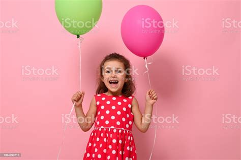 분홍색 드레스를 입은 생일 소녀는 분홍색 옷을 입고 화려한 풍선을 손에 들고 카메라를 바라보며 미소를 지으며 분홍색 배경에 복사