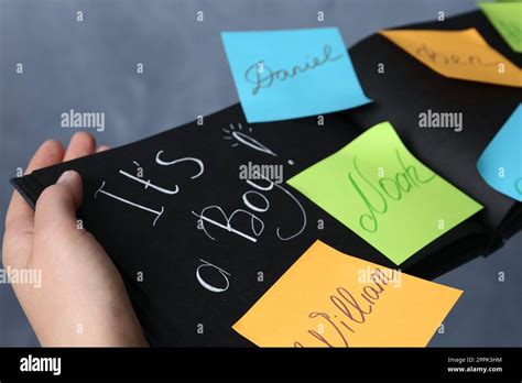 Woman Holding Notebook With Written Different Baby Names On Grey Background Closeup Stock Photo