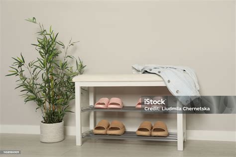 다양한 고무 슬리퍼 쌍과 홀의 흰 벽 근처에 아름다운 관엽 식물이 있는 세련된 보관 벤치 0명에 대한 스톡 사진 및 기타 이미지