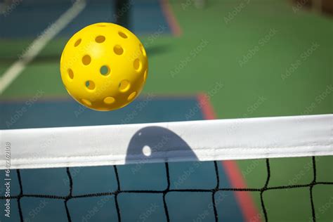 Yellow Pickleball Crossing A Pickleball Net With Shadow On The Top Tape