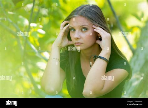 A Sad Girl Sits On A Background Of Foliage Holds Her Head With Her