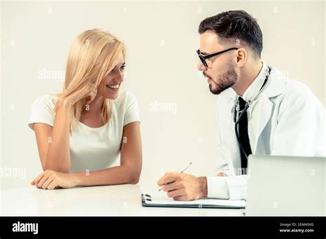 Male Doctor Talks To Female Patient In Hospital Office While Writing On