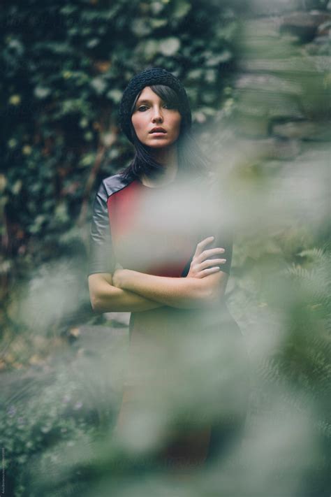 Stylish Woman With Arms Crossed Behind A Blur Of Leaves By Stocksy