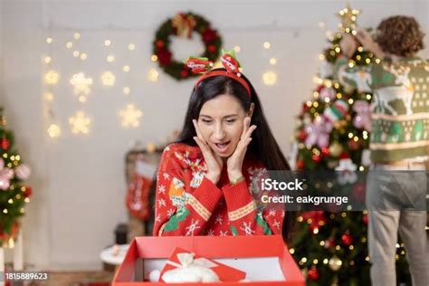 크리스마스 컨셉입니다 여자가 앉아서 놀랐고 크리스마스 트리 배경과 함께 선물 상자를 열었습니다 축제 분위기의 파티 12월에 대한