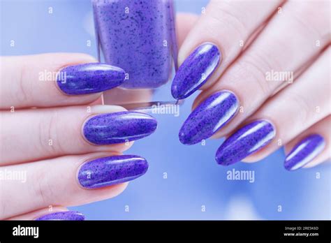 Female Hand With Long Nails And A Bottle Of Light Blue Lilac Color Nail