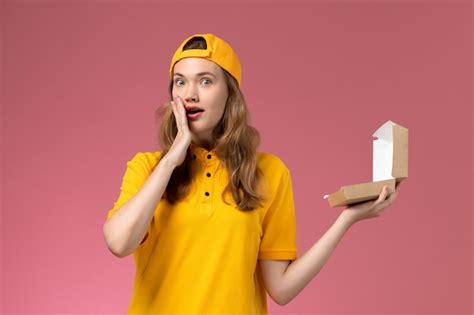밝은 분홍색 벽 작업 작업 서비스 배달 유니폼에 빈 작은 배달 음식 패키지를 들고 노란색 유니폼과 케이프 전면보기 여성 택배