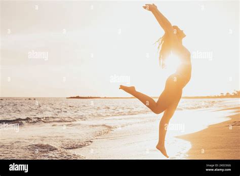 One Happy And Healthy Young Woman Jumping On The Sand Of The Beach