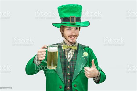 맥주와 미소의 녹색 세인트 패트릭 벌 들고 얼굴에 행복 한 젊은이의 그림 그는 큰 엄지손가락을 개최 회색 배경에 고립 St